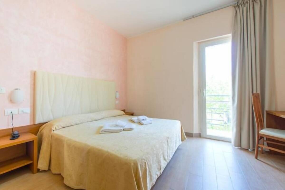 Quarto de hotel com cama, mesa de cabeceira, cadeira e vista para o exterior.