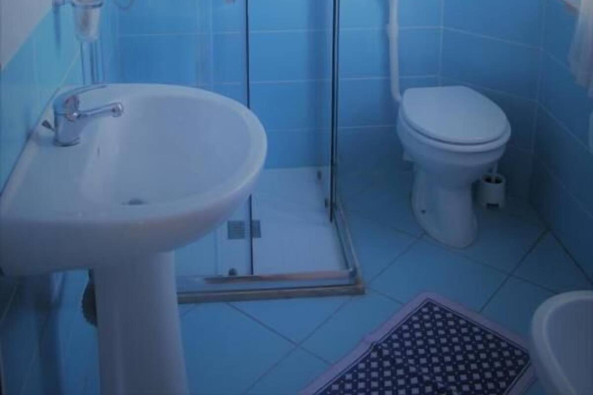 Casa de banho com cabine de duche em vidro, lavatório branco e sanita.