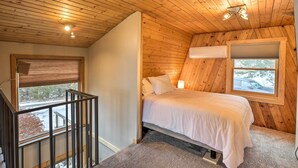 Quarto com teto de madeira, uma cama, janela e escada.