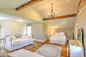Um quarto amplo com duas camas, um candelabro, uma toucador com espelho e uma viga de teto de madeira.