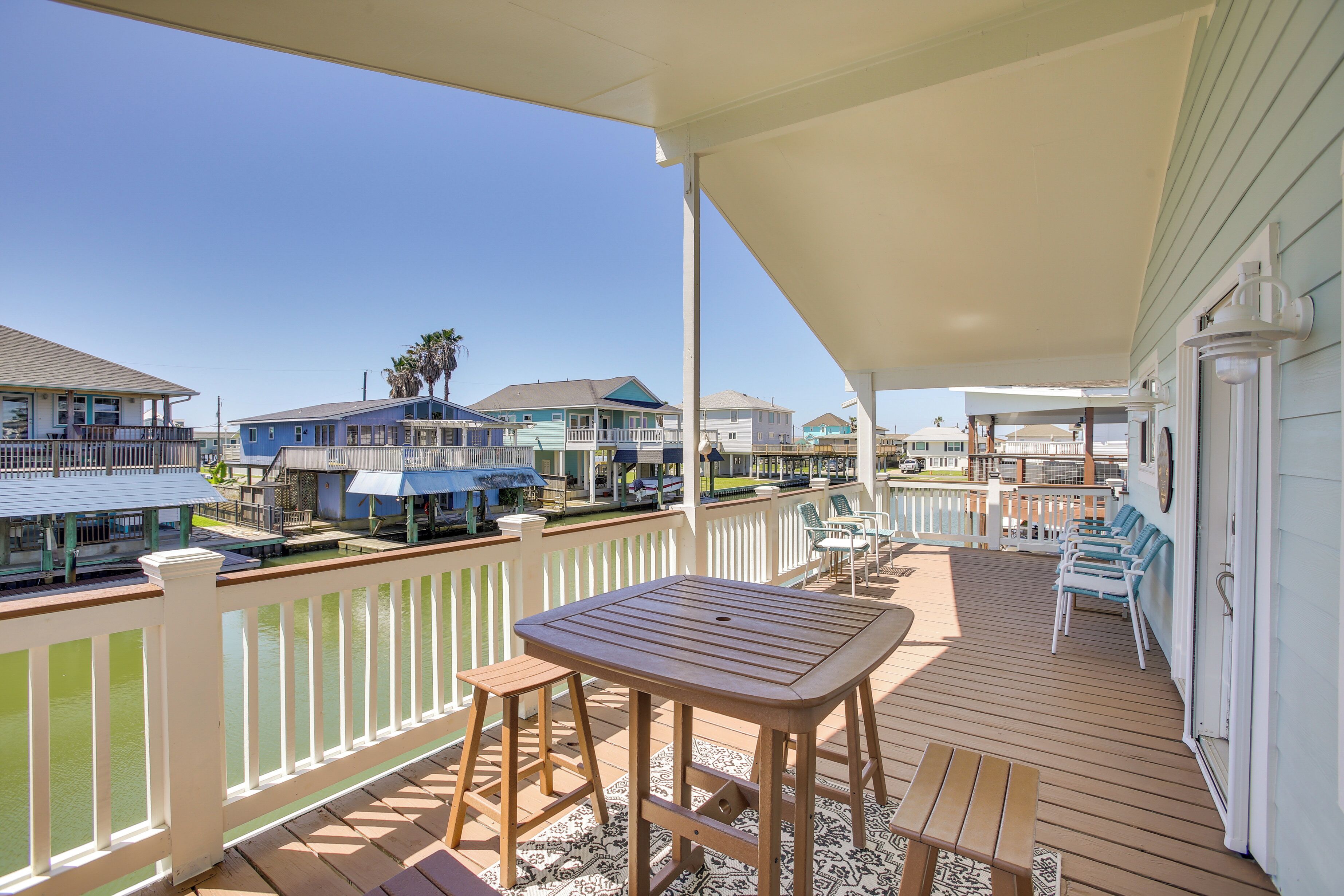 Um terraço coberto com mesa e cadeiras, com vista para uma marina com barcos e casas.