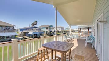 Um terraço coberto com mesa e cadeiras, com vista para uma marina com barcos e casas.