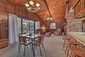 Interior acolhedor de uma cabana com mesa de jantar, cadeiras, um sofá e um espaço de bar.