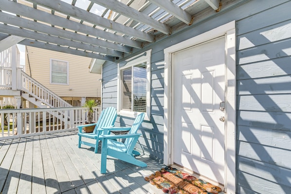 Um deck de madeira com duas cadeiras Adirondack azuis, uma porta branca e uma escadaria que leva a um andar superior.