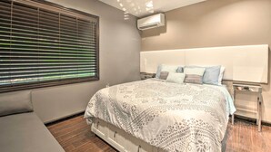 Quarto com cama grande, janela com persianas, ar-condicionado e mesa de cabeceira.