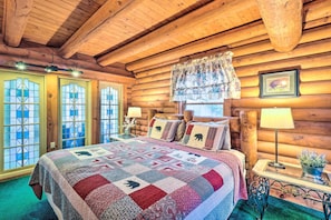 Um quarto de cabana de madeira com uma cama grande, duas janelas com cortinas, teto de madeira e um quadro na parede.