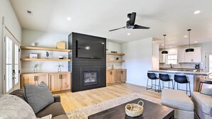 Uma sala de estar moderna com lareira, sofá, mesa de centro e cozinha com banquetas.