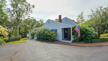 Uma casa térrea com varanda frontal, chaminé e uma bandeira americana.