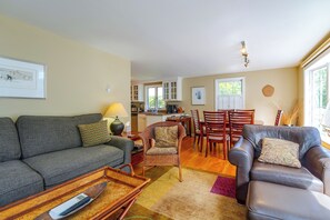 Uma sala de estar com um sofá cinzento, um sofá de couro marrom e uma área de jantar com cadeiras de madeira e uma mesa.