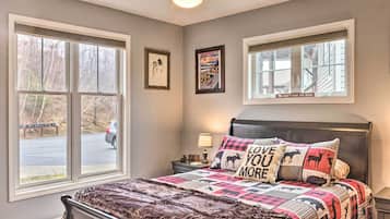 Quarto com cama grande, duas janelas, mesa de cabeceira e parede com quadros.