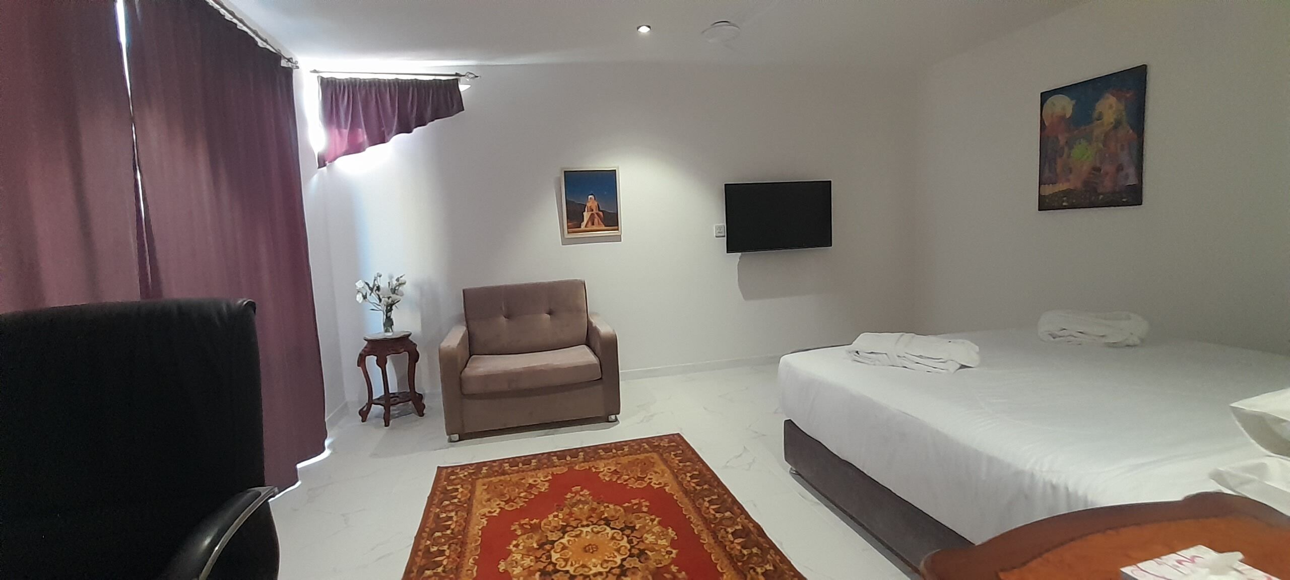 Quarto de hotel com uma cama, uma cadeira, uma televisão e um quadro na parede.