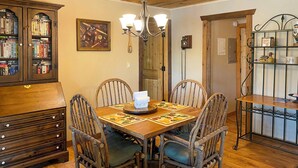 Uma sala de jantar com uma mesa de madeira, quatro cadeiras, um candelabro, um telefone antigo e uma estante de livros.