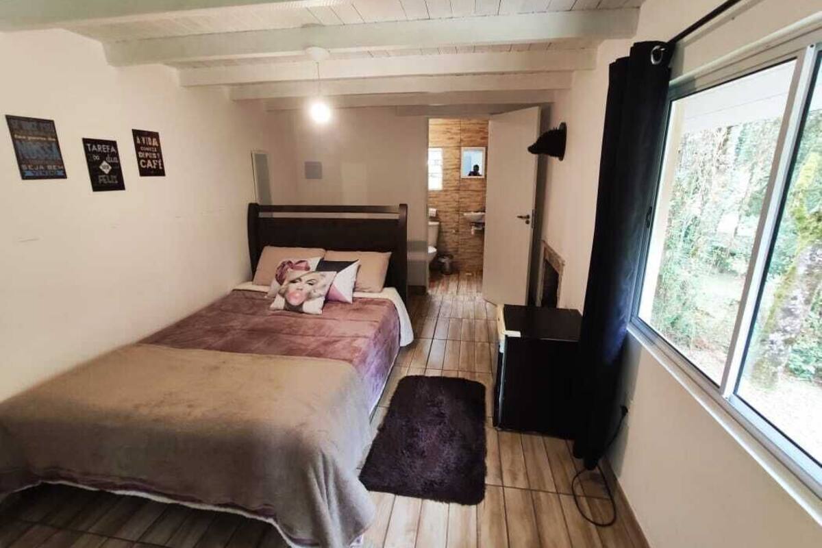 Um quarto com uma cama, uma janela, uma porta que dá para um banheiro e um tapete pequeno.