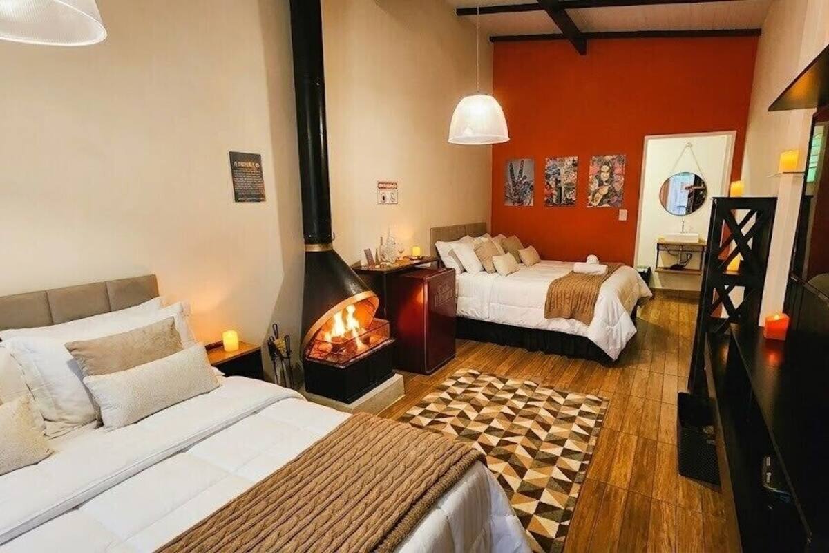 Quarto aconchegante com duas camas, lareira e uma luminária pendente moderna.