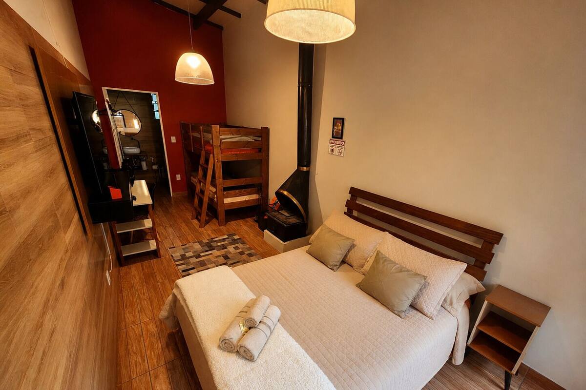 Quarto com cama, móveis de madeira, escrivaninha, cadeira, abajur e aquecedor fixado na parede.