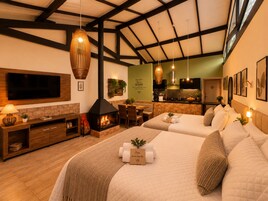 Quarto de hotel com lareira, televisão, área de refeições e cozinha compacta.