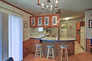 Uma cozinha com armários de madeira, uma ilha central com banquetas, um candelabro e uma geladeira.