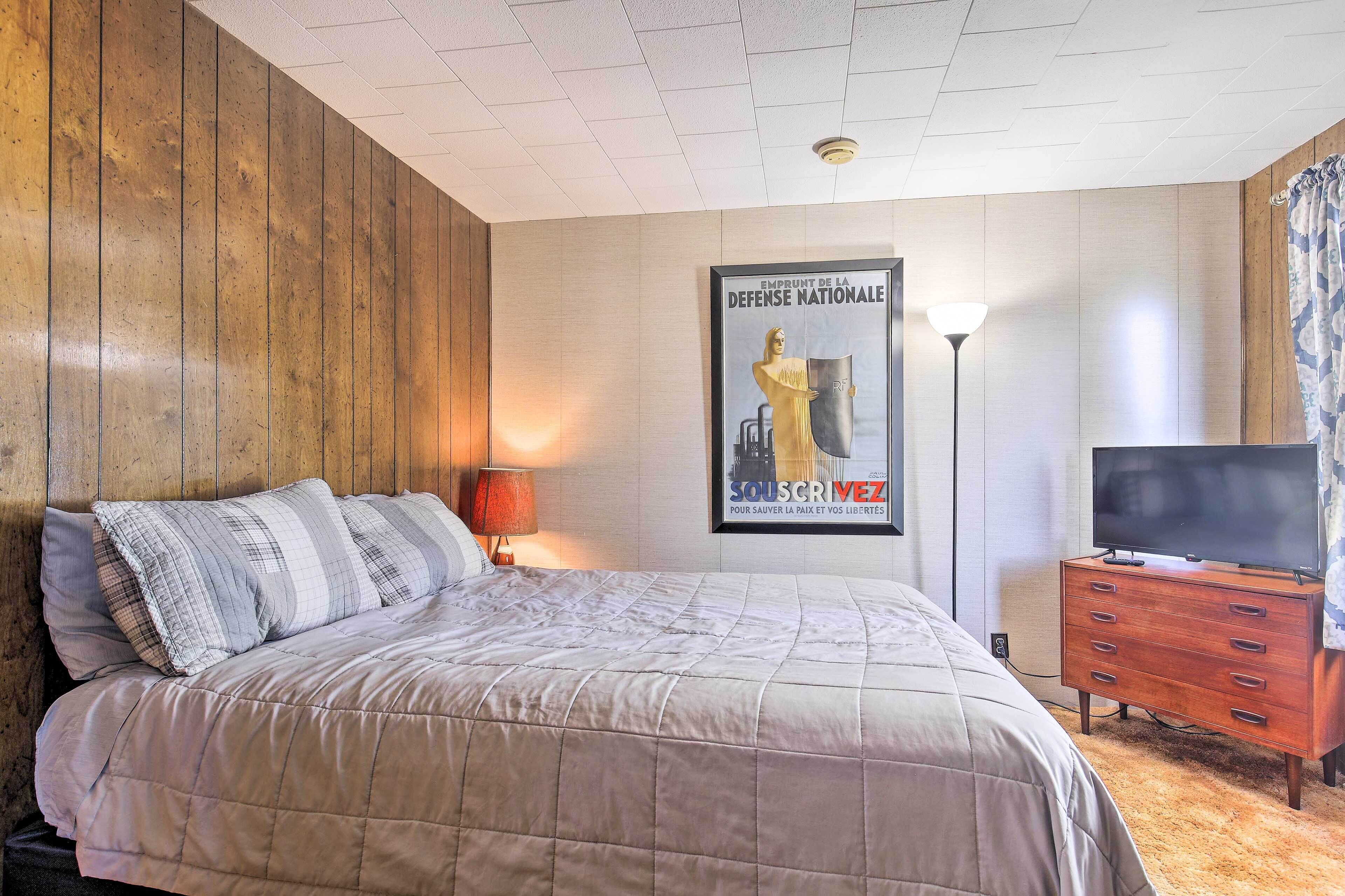 Um quarto com uma cama, penteadeira, luminária e um pôster na parede.