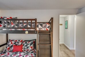 Uma cama beliche com roupa de cama estampada em padrão geométrico e uma escada de madeira.
