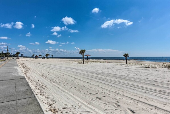 Uma praia com calçadão de concreto, palmeiras e céu azul límpido.