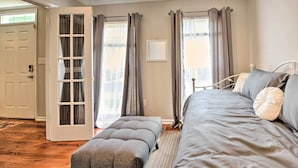 Quarto com cama, um banco e porta que dá para outro cômodo.