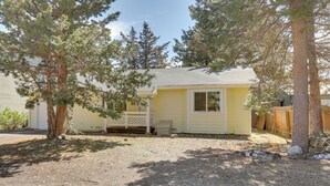 Uma casa amarela térrea com varanda coberta, rodeada por árvores e uma entrada de cascalho.