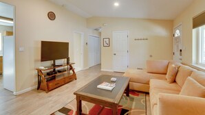 Uma sala de estar com televisão de tela plana, mesa de centro de madeira, sofá bege e tapete estampado.