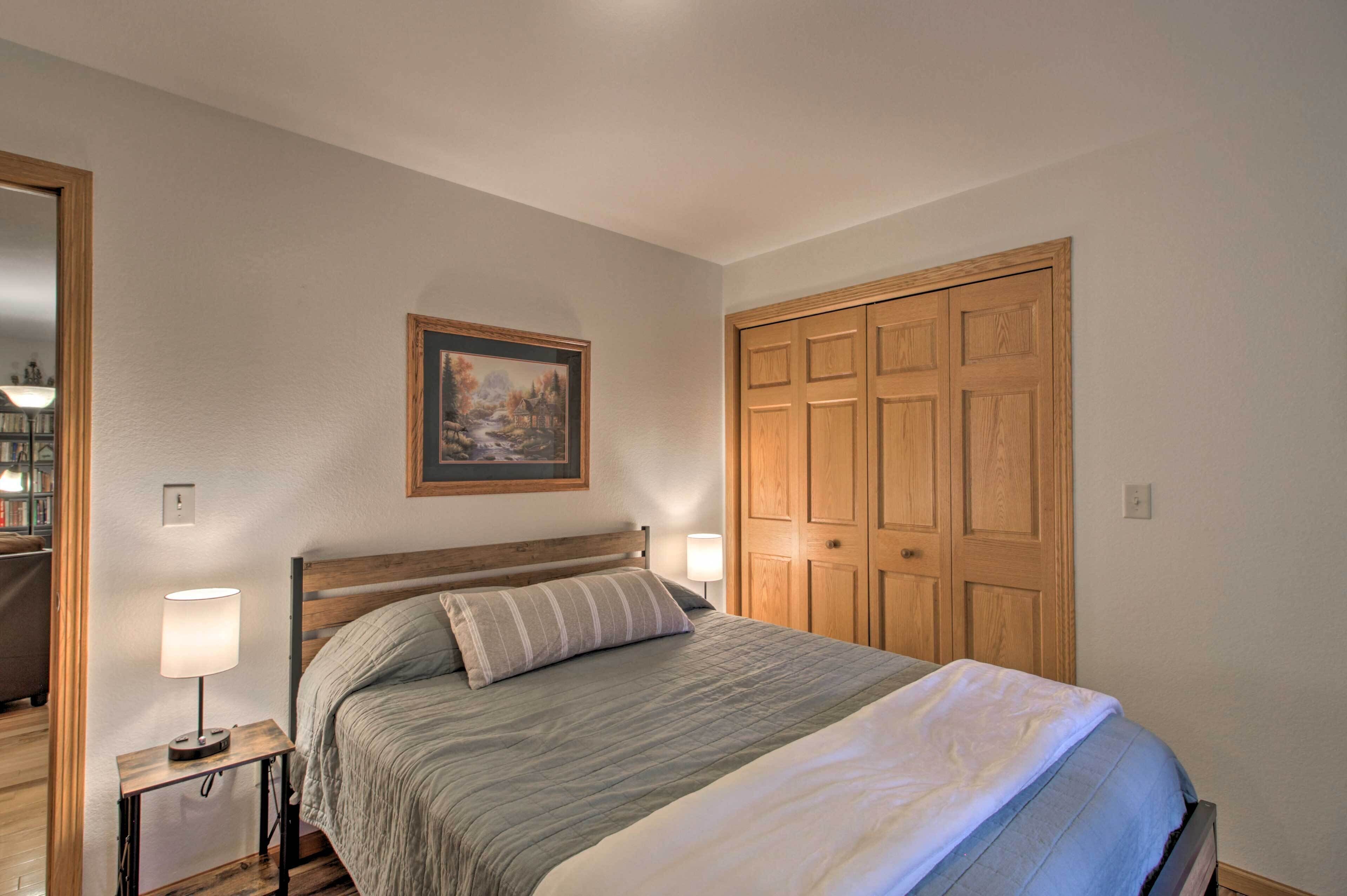 Quarto com cama, guarda-roupa de madeira, quadro emoldurado na parede e mesa de cabeceira com luminária.