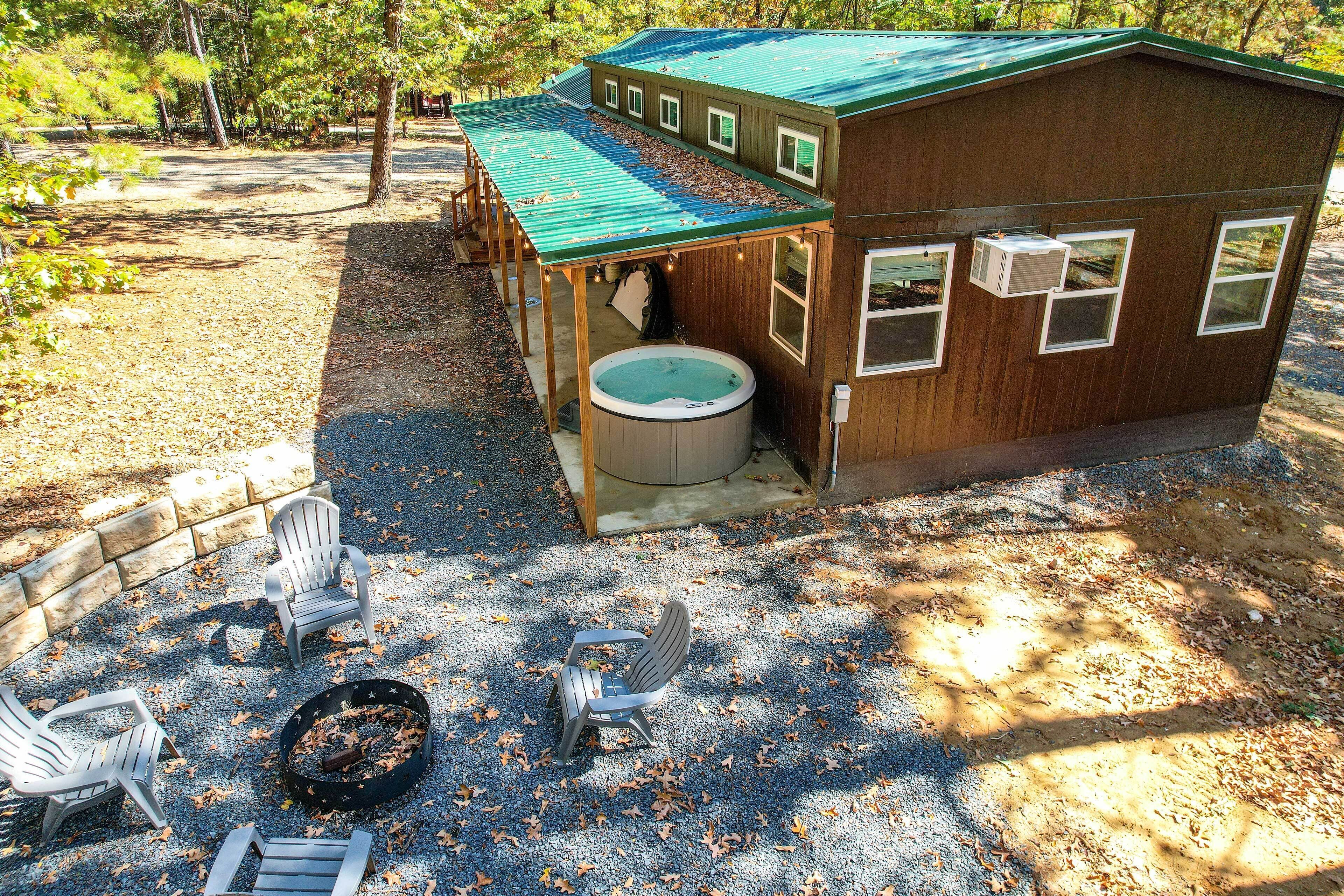 Uma cabana de madeira com telhado verde, hidromassagem e área de estar externa com cadeiras Adirondack.