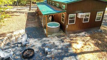 Uma cabana de madeira com telhado verde, hidromassagem e área de estar externa com cadeiras Adirondack.