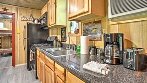 Cozinha com armários de madeira, geladeira preta, fogão, pia, cafeteira e torradeira.