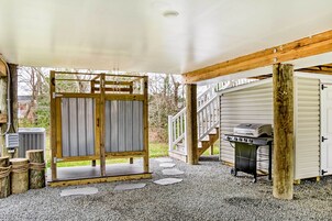 Uma área externa coberta com deck de madeira, churrasqueira e porta de garagem.