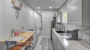 Uma cozinha moderna com uma mesa de jantar de madeira, banquetas de bar, forno embutido e máquina de café.