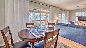 Uma sala de jantar com mesa redonda, cadeiras e vista para o exterior através de grandes janelas.