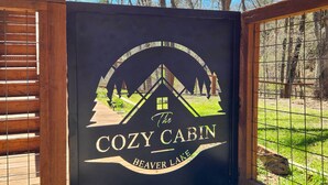 Placa para The Cozy Cabin em Beaver Lake, com ilustração de uma cabana e o nome.