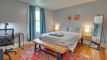 Um quarto com cama, escrivaninha, cadeira, espelho e janela com cortinas.