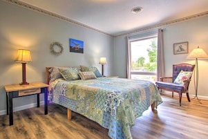 Quarto com cama, duas luminárias de cabeceira, uma cadeira, janela com cortinas e parede com grinalda e um quadro.
