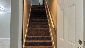 Escada carpetada com corrimão, levando a uma porta.