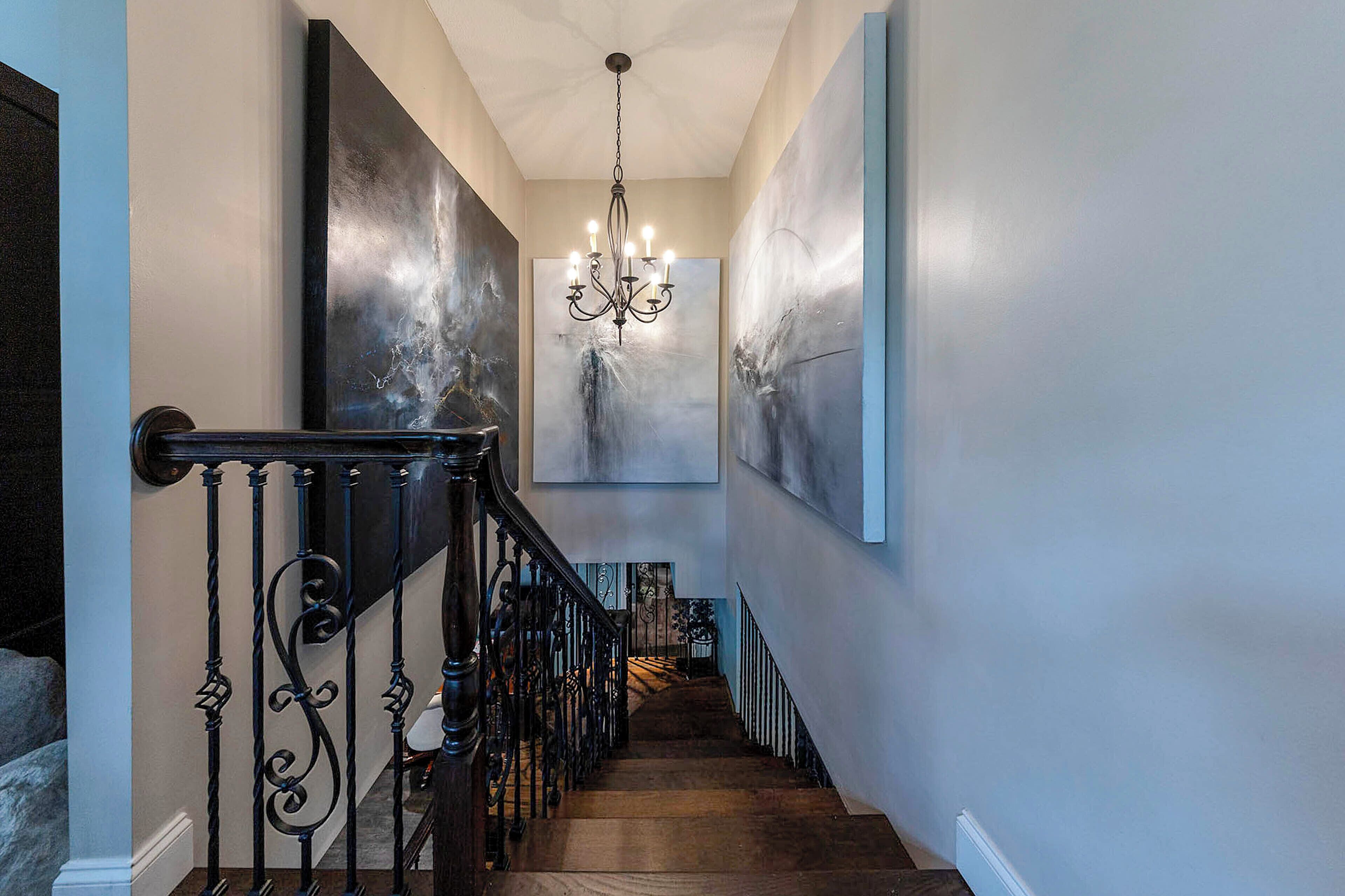 Uma escadaria com um candelabro, corrimãos de ferro preto e grandes quadros abstratos nas paredes.