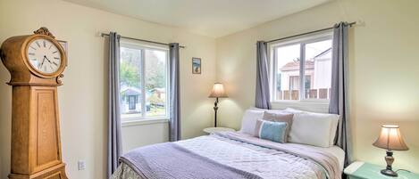 Quarto com cama, relógio de madeira, abajur e janela com cortinas.