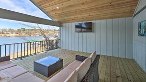 Um terraço coberto ao ar livre com piso de madeira, uma televisão de tela plana na parede e vista para um corpo de água.