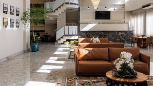 Um lobby espaçoso com um lustre imponente, uma escadaria e uma área de estar com uma mesa de centro.