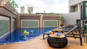 Uma área de piscina no terraço, com cadeiras de descanso e uma mesa redonda com comida e bebidas.