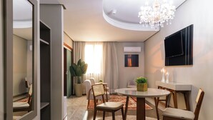 Uma sala de estar moderna com uma mesa de jantar redonda, cadeiras de madeira, um candelabro, uma televisão de tela plana e um vaso com planta.