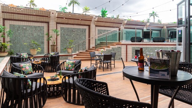 Uma área de pátio externa com mobiliário de vime, um bar e vista para a piscina.