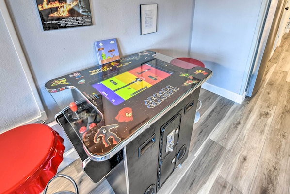 Uma mesa de jogos de fliperama retrô com design colorido e um banquinho vermelho.