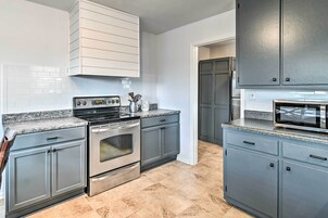 Cozinha com armários cinza, forno de aço inoxidável, micro-ondas e painel de azulejos.