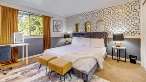 Quarto de hotel com uma cama grande, duas mesas de cabeceira, uma escrivaninha, uma cadeira e uma janela com cortinas.