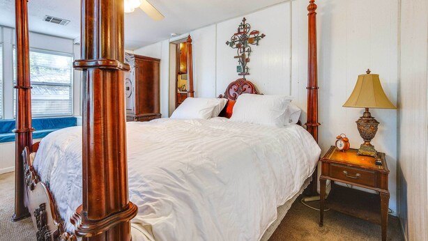 Uma cama grande com cabeceira de madeira, mesa de cabeceira com abajur e um detalhe decorativo na parede.