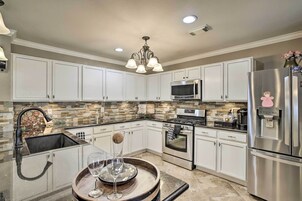 Uma cozinha moderna com armários brancos, eletrodomésticos de aço inoxidável, painel de backsplash de pedra e um candelabro.